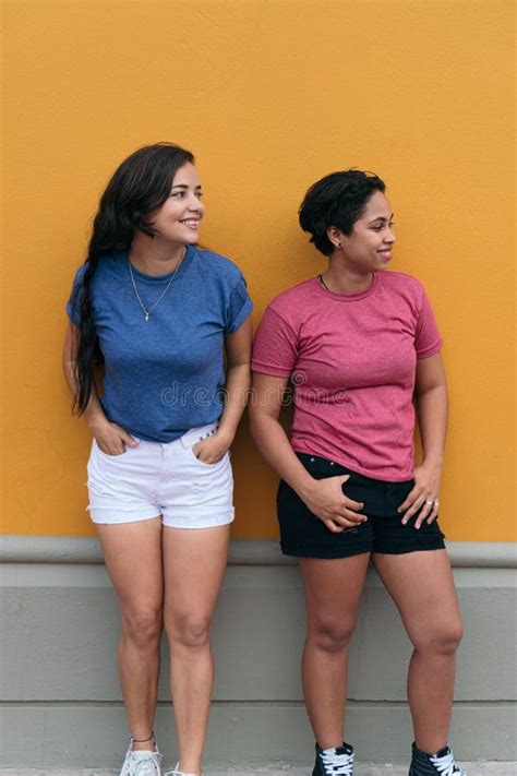Two Latina Friends Standing On A Yellow Wall Stock Image Image Of