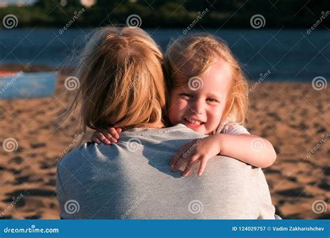 Beautiful Blonde Mom And Daughter Cuddling On The Beach At Sunset