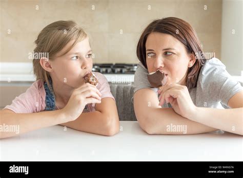 Mother With Her 12 Years Old Daughter Sitting In The Kitchen Eating Ice