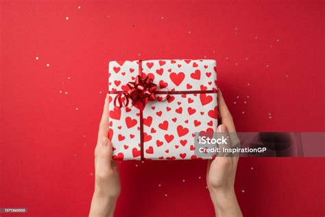 발렌타인 데이 장식 반짝이는 스팽글 핸즈가 하트 패턴이있는 흰색 포장지에 선물 상자를 들고 있는 1 인칭 탑 뷰 사진과 카피