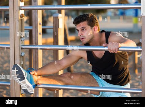 Male Athlete Stretching Legs On Outdoor Fitness Station After Strength