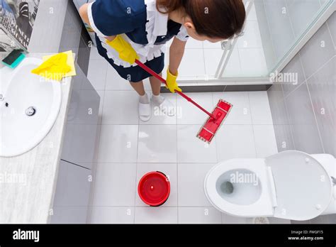 Housekeeper Or Maid In A Neat Uniform And Apron Standing Mopping The