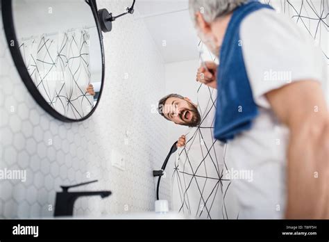 An Adult Hipster Son And Senior Father In Bathroom Indoors At Home