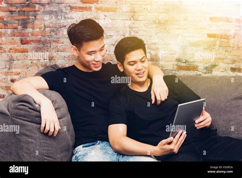 Asian Gay Couple Watching And Looking At Phone Tablet Together