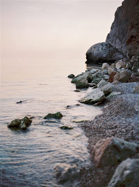 blue and pink sunset above the sea with rocks coloured in pink because