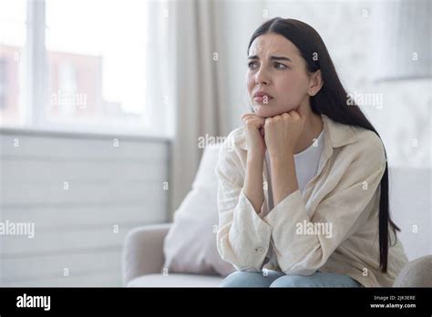 Depressed Woman Near Window Sitting On Sofa At Home Disappointed And