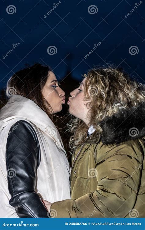 A Lesbian Couple Kissing Each Other With Puckering Lips At Night In The