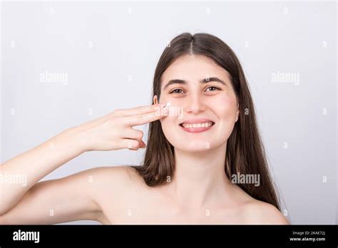 Excited Young Woman Spreads Moisturizing Cream On Her Cheek Looking