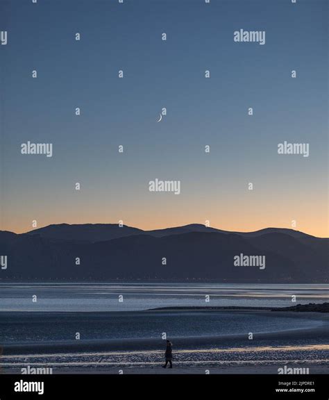 An Unidentifiable Couple Take An Evening Stroll Along The Beach By The