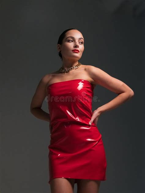 Young Pretty Brunette Woman Poses In Stylish Red Latex Dress And Chain