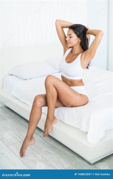 Beautiful Young Woman Wearing White Lingerie Sitting On Bed Stretching