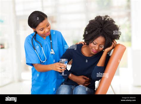Caring Young African American Nurse Offering Sick Patient Water Stock