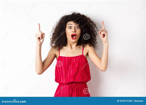 Impressed Young Woman With Curly Hair Wearing Red Dress Gasping And