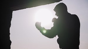 Silhouette of a boxer against the backdrop of a beautiful sunset and a river in an abandoned building, trains blows on a punching bag. Epic video. Motivation. Sports and martial arts. Slow motion.