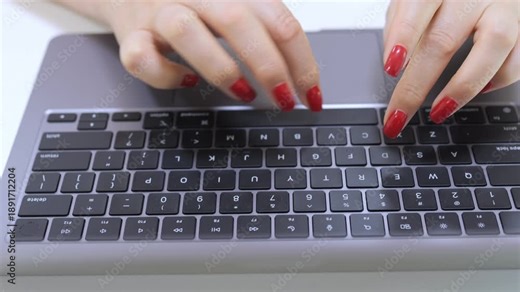 Woman is typing on a laptop keyboard with red fingernails. The keyboard has a number pad and a space bar