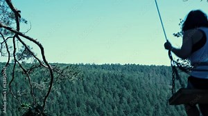 Extreme swing.A girl swings on a swing over a cliff against the background of a forest