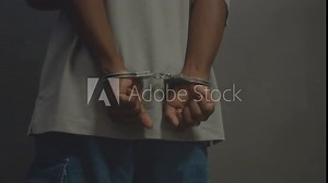 Midsection back view of unrecognizable arrested Black man keeping handcuffed hands behind his back in dark roomMidsection back view of unrecognizable arrested Black man keeping handcuffed hands behind