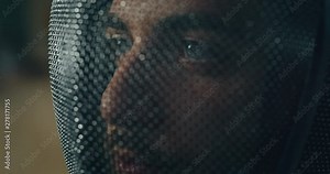 Slow motion close up of an young man professional fencer with blue eyes with protection mask before start practising assaults of fencing in a gym.