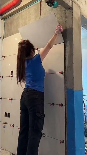 the process of installing rectangular white ceramic tiles on the walls in a room in a building