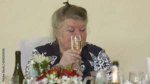 Senior woman at festive dinner table. Seniors celebrating 70th birthday in restaurant. Happy elderly woman holding a glass of champagne and talking with friends.