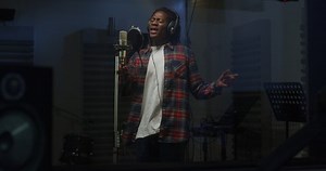 Portrait of a Professional Male Black Singer with Headphone Recording a Song in a Studio. African Young Artist Performing his New Romantic Single, Singing Emotionally with an Expressive Face