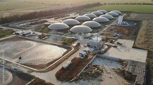 Biogas plant surrounded by nature. Modern storage tanks on biogas farm on field. Renewable energy from biomass. Aerial view. Energy source.