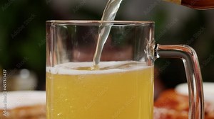 Pouring beer in glasses close-up. Traditional German Cuisine. Smoked sausages with fried potatoes, pickled cucumbers, bratwursts and fresh pretzels on table. Cooked National Czech Food.