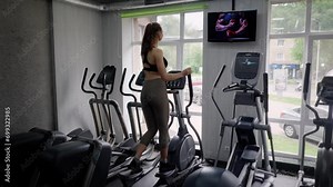 A young slender woman in excellent athletic shape enters the gym and customize the operation of the leg exercise machine. Hand movement and pedaling. The concept of sports lifestyle and healthy