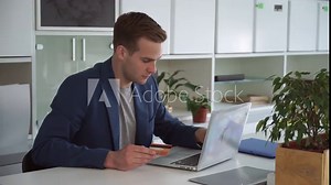 Man typing number debit card on the computer. He happy and smile looking to the camera. Male wearing in blue suit. Online banking at the working place.