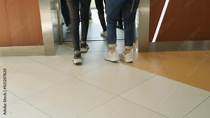 A dynamic first-person view captured with a handheld camera, showing the lower half of various people walking into an elevator. The scene focuses on the movement and diversity of footwear