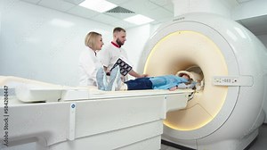 Woman doctor radiologist explains good results of CT scanning for young female patient, showing the snapshot with images, observing and analyzing CT scan in modern clinic beside modern CT scanner