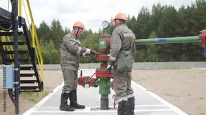 Oil field technical workers opening or closing valve of wellhead. Injection tree is destined for injection wells sealing and their operating regime regulation. Oil industry