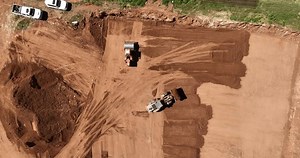 Aerial footage of a loader and a vibratory soil compactor working on a construction site and preparing the area for construction work. Filmed in C4K Apple ProRes 422 HQ