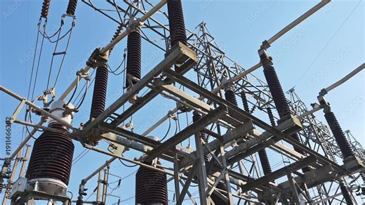 Low angle panning right video view of high voltage electrical power substation switchyard structure with disconnect switch and insulator equipment under blue sky.