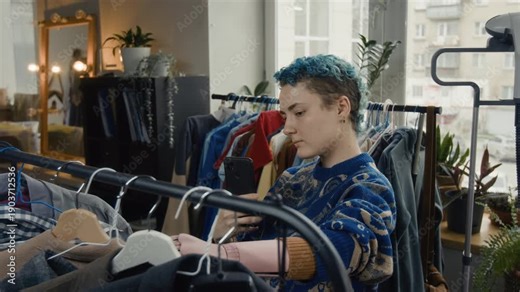 High angle shot of young woman taking pictures of secondhand clothes, helping with her prosthetic arm whie working as promo manager of thrift shop