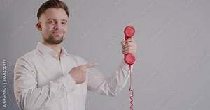 Man posing with red landline telephone receiver, demonstrating anold-fashioned way of communication. Man presents retro handset as symbol of traditional communication in world of modern technology.