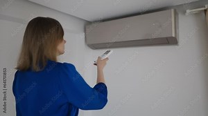 Woman holding remote control aimed at the air conditioner.
