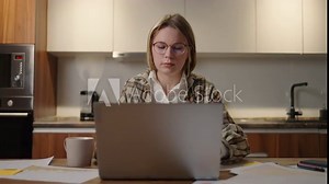Zoom camera A woman with glasses works remotely from home sitting at a table with a laptop and a felt-tip pen marks the data on the graph. Distance learning student at home to perform an assignment