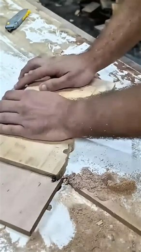 smoothing a brown wooden plank manually using a sharp metal tool in a professional workshop project