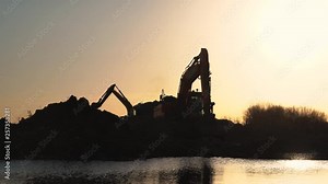 Silhouette of excavator. Dredge digs ground and loading tipper. Digger machine digging hole. Excavation of canal. Dump truck,tracked,bagger,backhoe,shovel,sunny blue sky,sun in background,backlight.