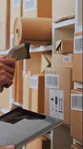 A worker scans barcodes on various packages in a neatly organized storage area filled with boxes. The individual uses a handheld scanner, ensuring proper inventory management