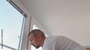 The man is drilling a hole in the window. Blinds installation.