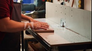 Woodworking expert wears protection gear, inserting plank in spindle moulder next to coworker. CNC machinist uses safety glasses while cutting lumber with wood shaper helped by colleague, camera A
