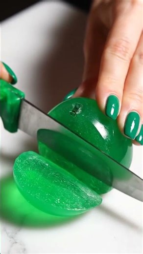 A chef's knife glides through glass on marble, revealing crystalline textures under soft lighting.