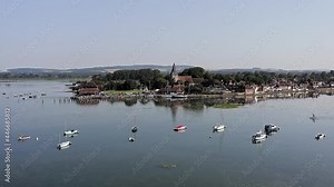 Bosham estuary full of boats reflecting on the calm water and with Paddle Boarders navigating between boats. Aerial footage.