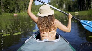 Beautiful young woman kayaking on lake. Girl rowing oars on a kayak on the river. Sports hike, water rafting in nature.