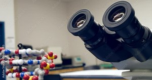 A student in a college biology science classroom doing an experiment behind a microscope and a dna double helix model.