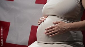 Unrecognizable future mother expecting baby on Swiss national flag background. Pregnant woman touching belly. Demography, population in Switzerland.