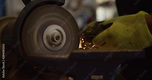 Front side view of metal being shaped by bench grinder, igniting sparks 4K slow motion