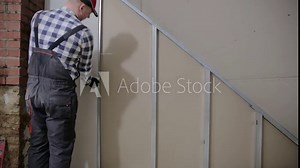 Man installing plasterboard sheet to wall for attic room construction